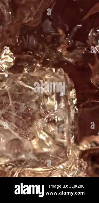 Ice falls into a glass of whiskey. Filmed on a high-speed camera at ...