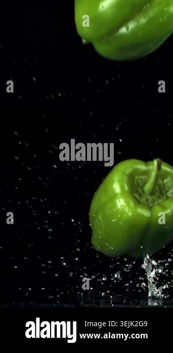 Green peppers bouncing and splashing on reflective black surface ...