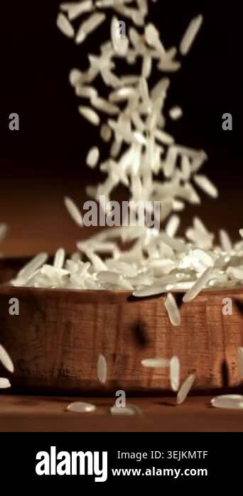 White rice falls into a wooden bowl. Filmed on a high-speed camera at ...