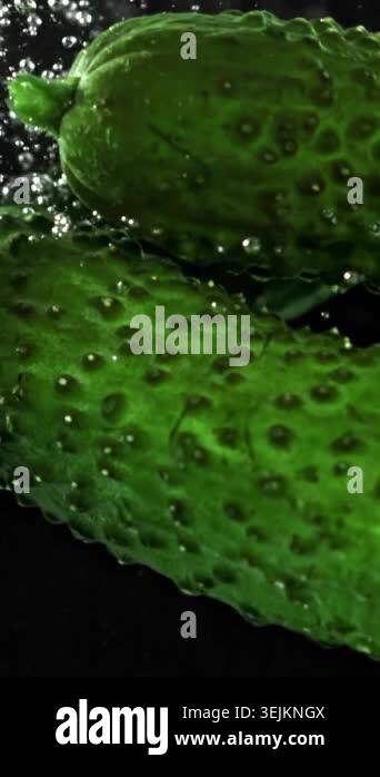 Cucumbers falling under water on a black background. Filmed on a high ...