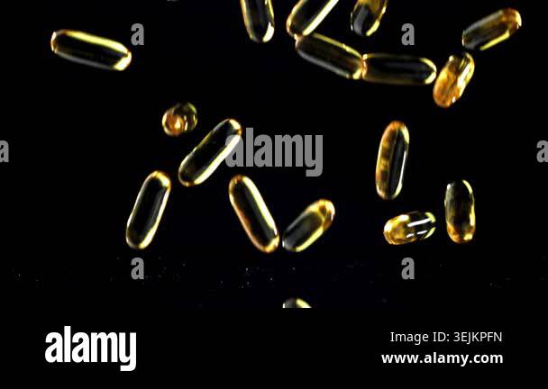 Gold oil capsules on black background, warm amber glow and translucent ...