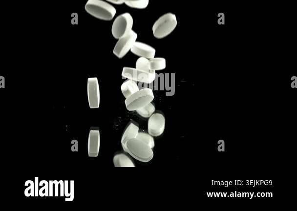 White tablets scattering across reflective black, dynamic closeup ...