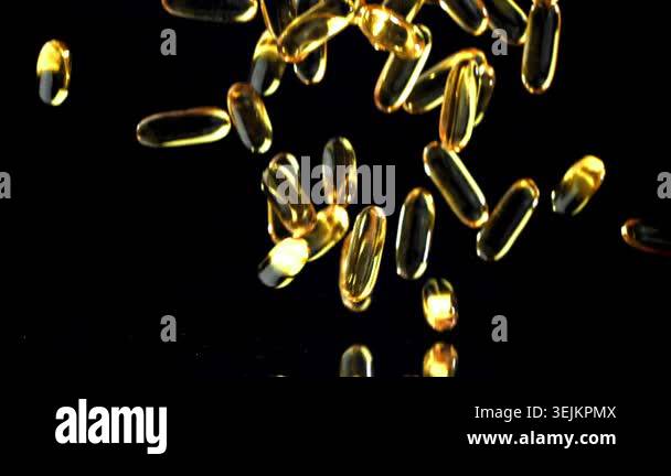 Golden softgel supplements falling on black reflective surface, Filmed ...