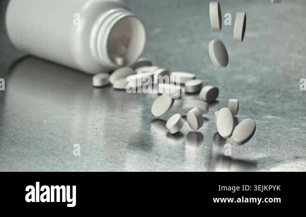 White tablets pour from overturned bottle onto reflective metal Filmed ...