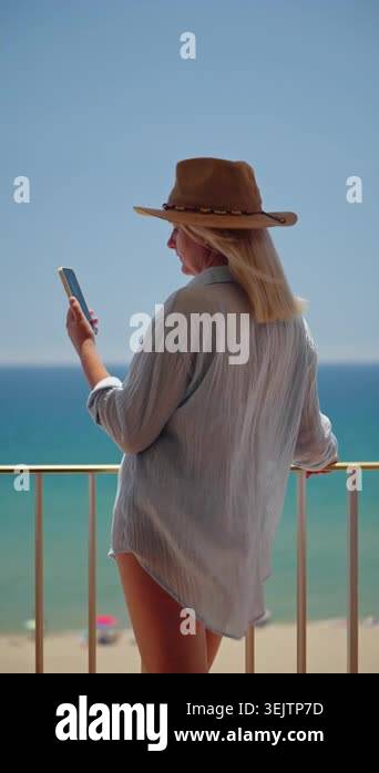 Woman using smartphone on balcony with beach and sea view during sunny ...