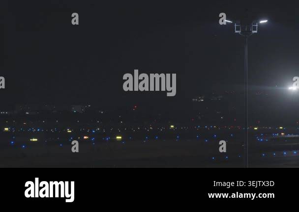 Dark airport apron at night with rows of blue taxiway edge lights and a ...