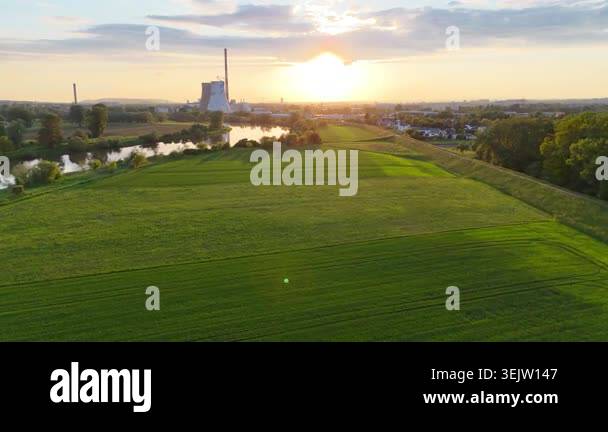 Aerial view of lush green fields and a river at sunset, with a power ...