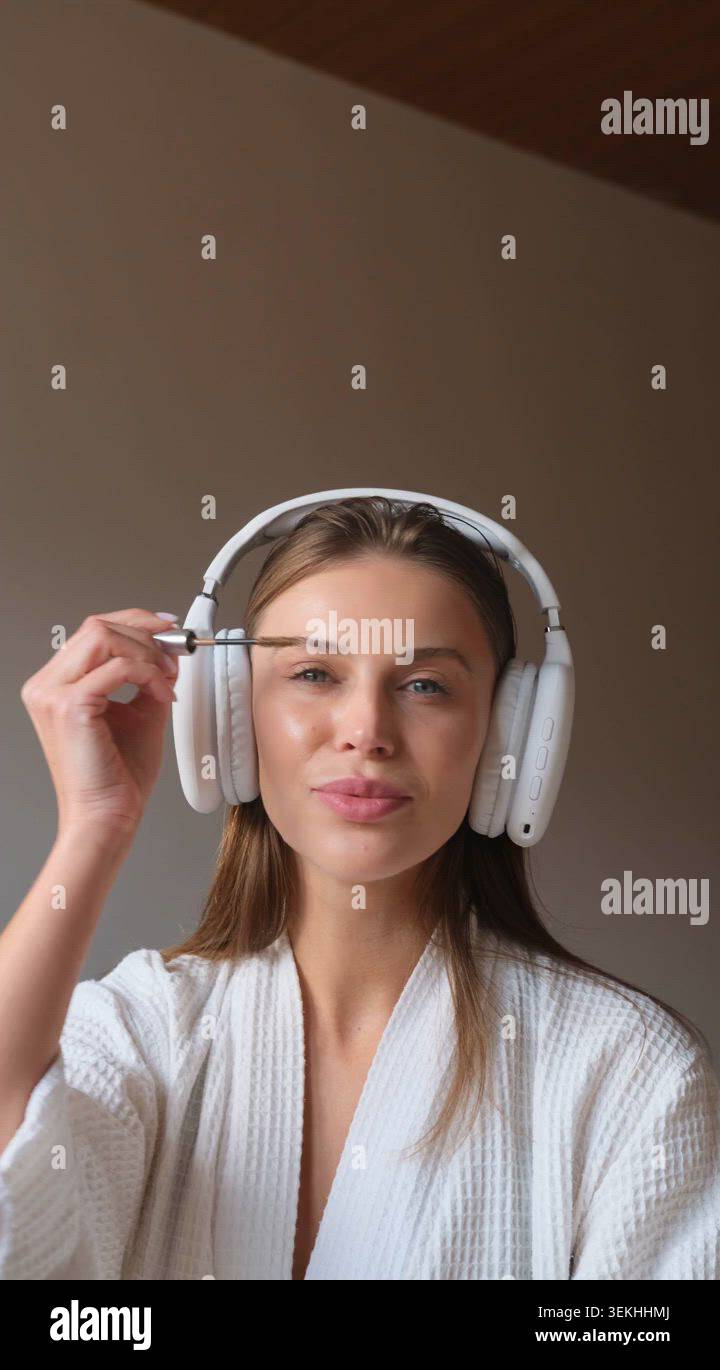 Smiling woman shaping her eyebrows while wearing white headphones Stock ...