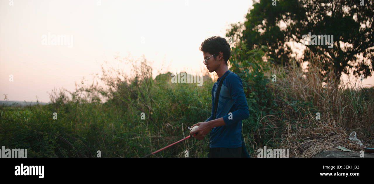 Young fisherman casting his fishing rod into a river at golden sunset ...