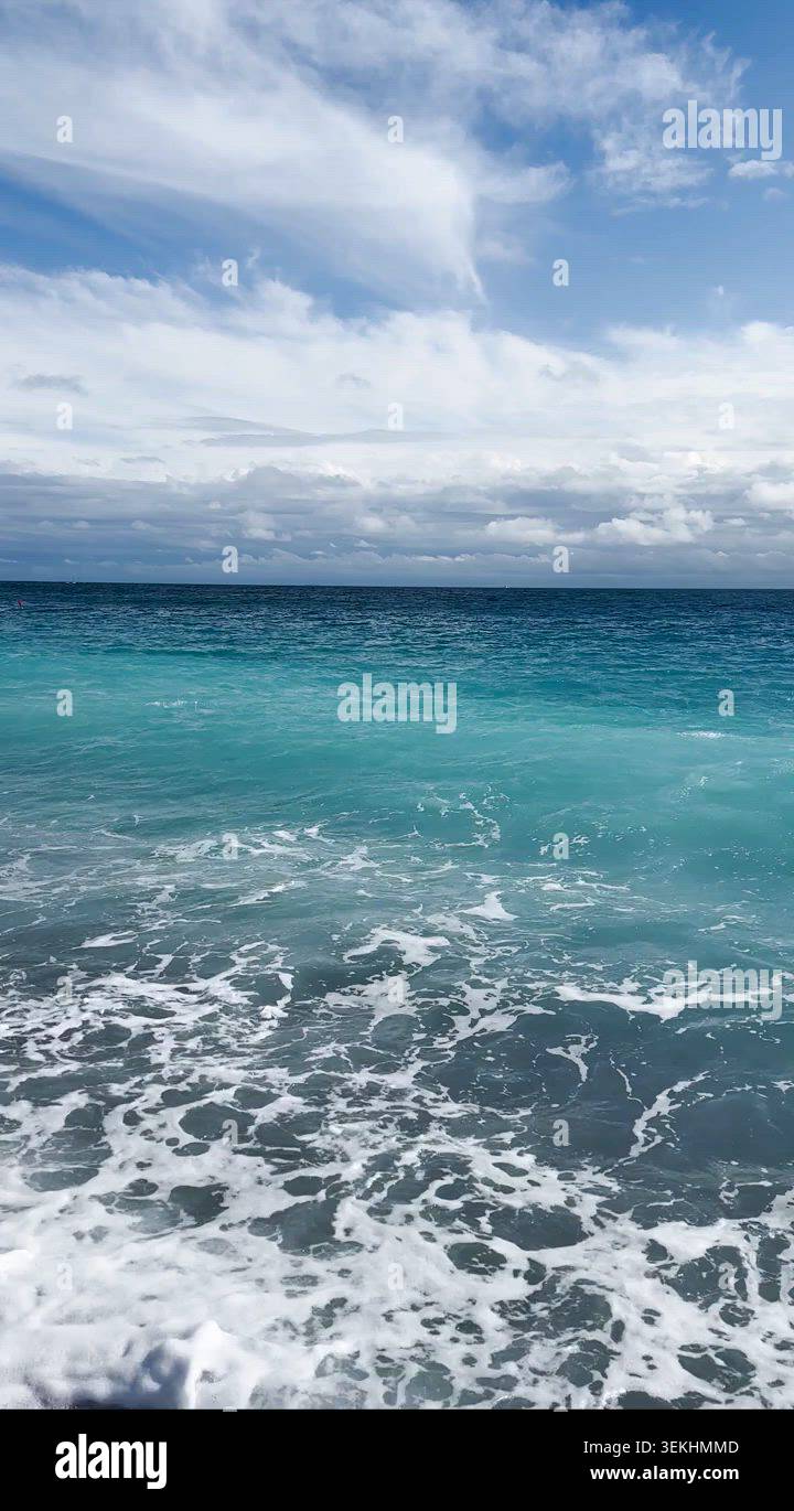 Turquoise sea wave splash foam on a sandy beach closeup and blue sky ...