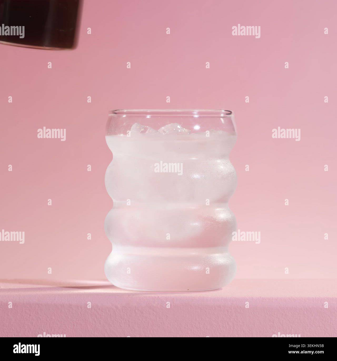 Pouring iced coffee into a unique wavy glass with ice cubes on a pink ...