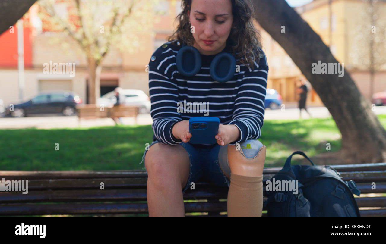 Amputee woman with prosthetic leg using smartphone in a park Stock ...