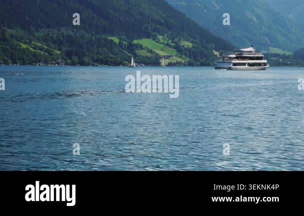 Passenger boat moving across lake water with mountains and shoreline in ...