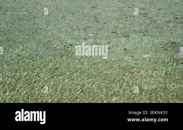 Clear shallow water with visible ripples moving across a pebble-covered ...