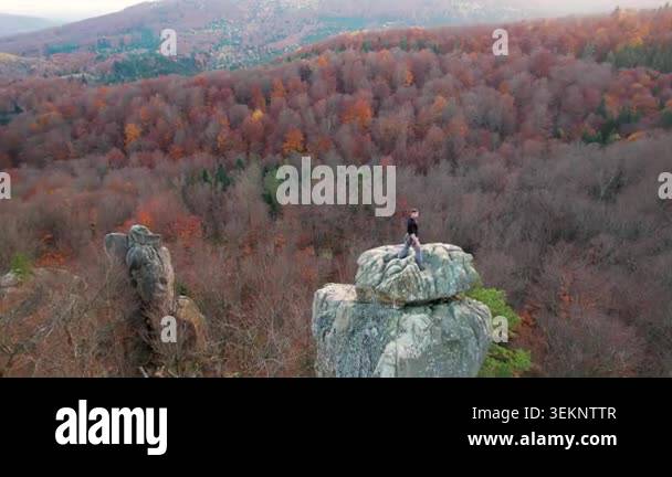 Male climber stands on top of rock in evening light, enjoying forest ...