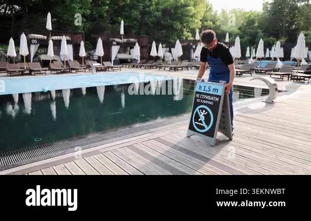 Hotel staff ensuring pool safety, placing a no jumping sign near a ...
