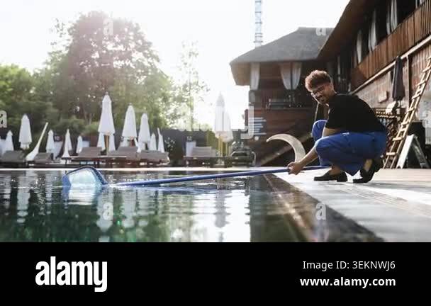 Worker cleaning a swimming pool, extending a skimmer pole into the ...