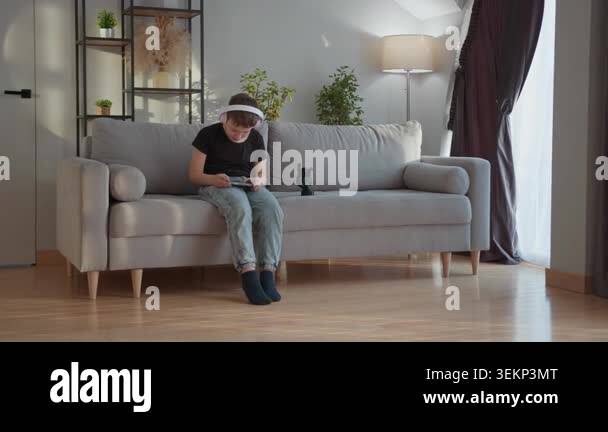 Young boy wearing headphones joyfully dances in living room holding ...