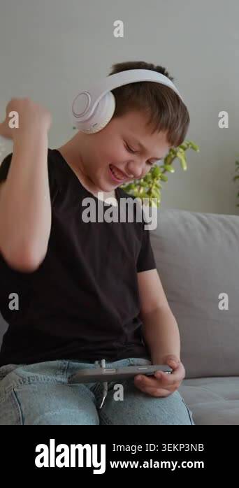 Young boy wearing headphones plays mobile game on couch, showing ...