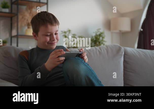 Young boy engrossed in mobile gaming while relaxing on a comfortable ...