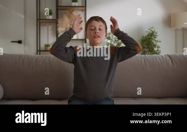 Young boy sitting on sofa, hands on head, screaming in frustration and ...