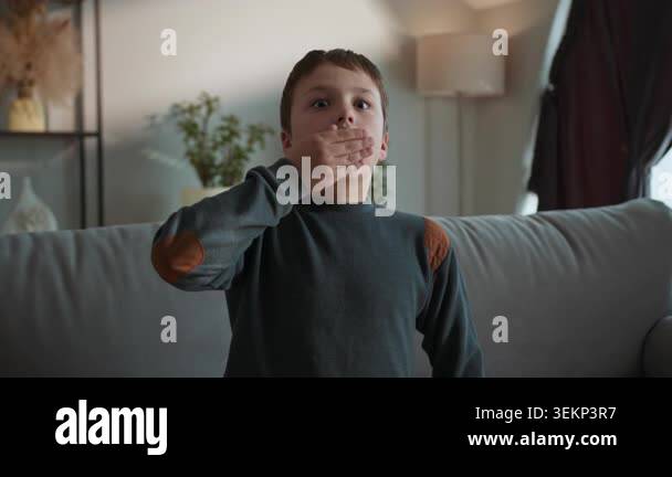 Young boy with wide eyes covers his mouth in surprise or shock while ...