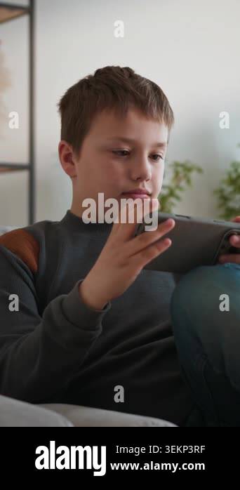 Young boy engrossed in mobile game on couch, smiling with enjoyment and ...