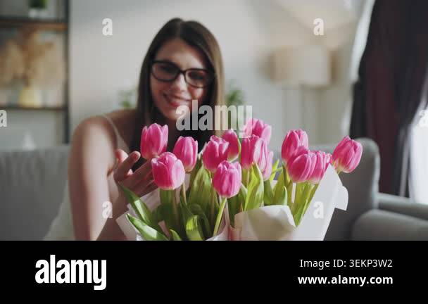 Young woman with glasses happily smelling a bouquet of vibrant pink ...