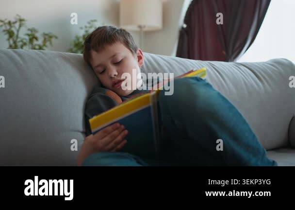 Young boy rests head on sofa cushion, eyes closed, holding open ...