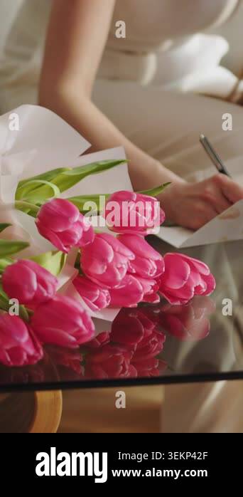 Close-up of womans hands writing on paper with pen, pink tulips in ...