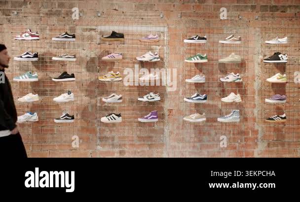 A young man walks past a brick wall with various sneakers displayed on ...