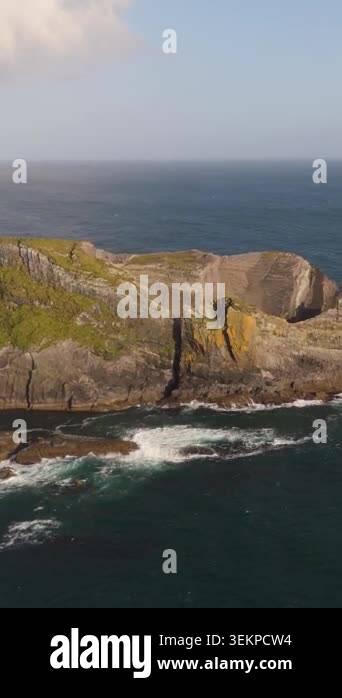 The rugged cliffs stand against the vast expanse of the ocean, enduring ...
