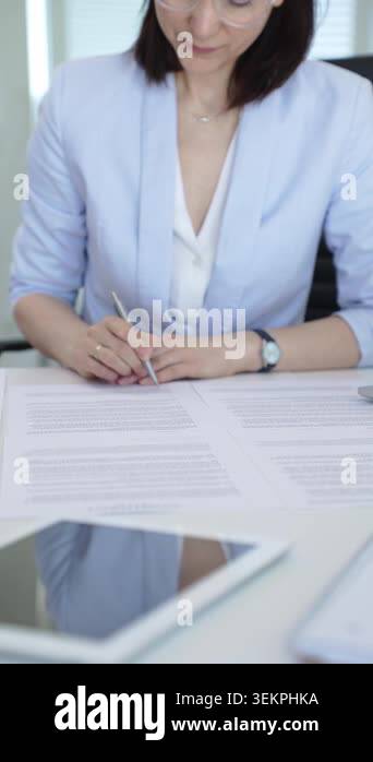 Businesswoman signing a contract at a modern office desk, pen in hand ...