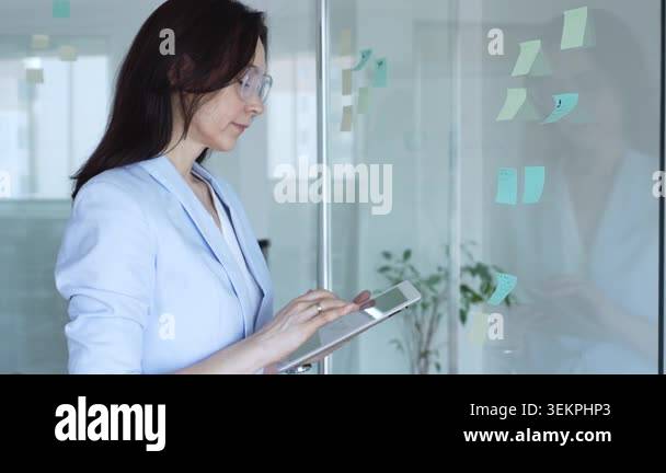 Businesswoman arranging sticky notes on a glass board, brainstorming ...