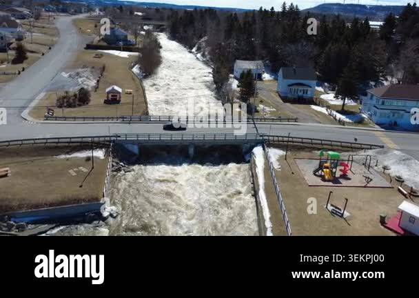 Drone footage flying upstream above a flooded spring river beneath road ...