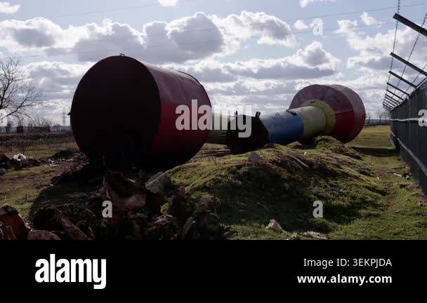 Colorful industrial tanks are seen lying on the ground in a grassy area ...