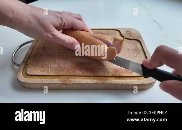 Slicing a boiled sausage on a wooden cutting board on a white table ...