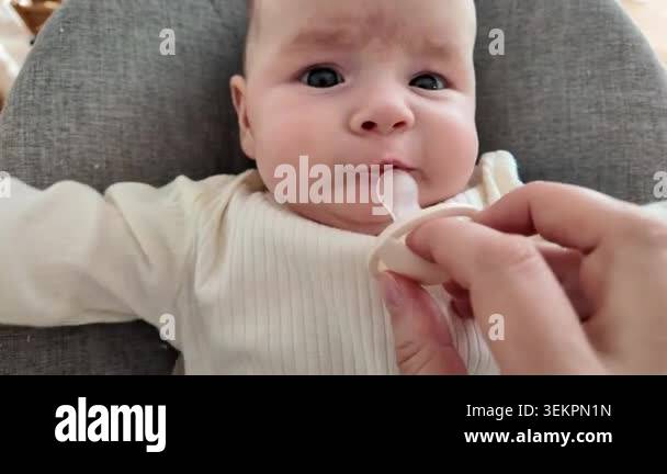 A parents hand gives a silicone pacifier to a small baby. The infant ...