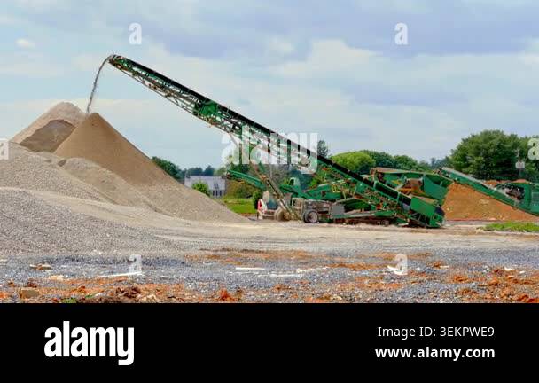 Workers operate a conveyor system that moves gravel to a large pile at ...