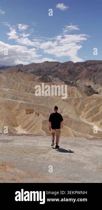 Vertical Screen: Man in black shirt walks toward dramatic eroded ...
