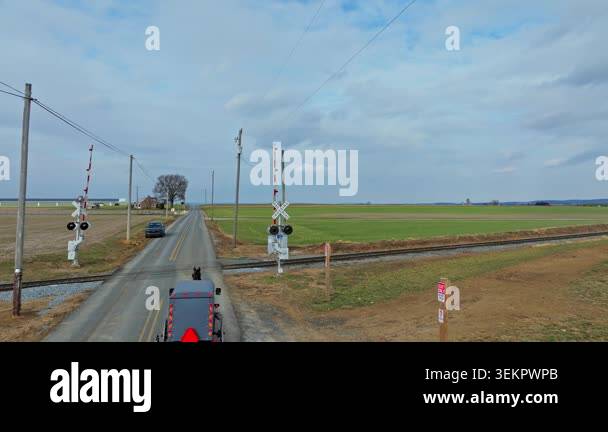 A horse and buggy cross rail road track crossing gate lowers as cars ...