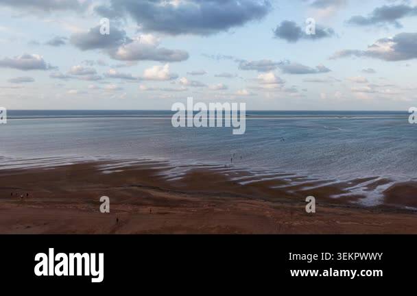 Wide coastal view with low tide, wet sand, calm sea and soft clouds in ...