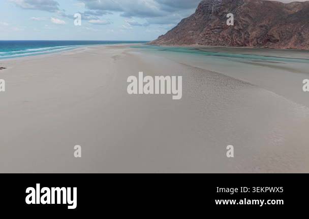 Wide sandy beach with turquoise shallow water and distant rocky ...