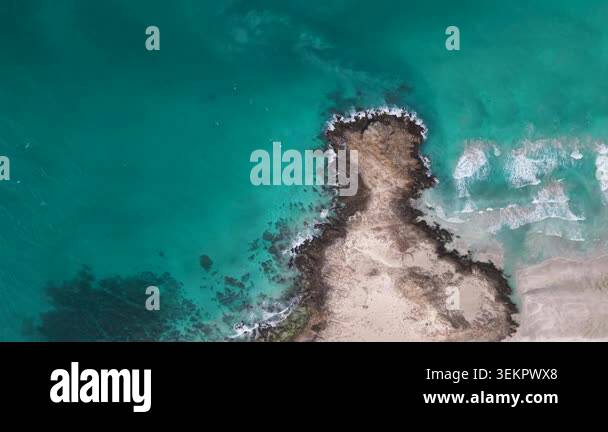 Aerial view of rugged rocky shoreline with waves breaking into clear ...