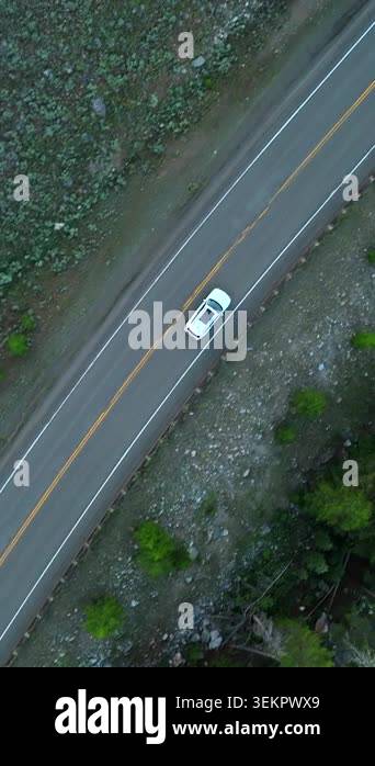 Vertical Screen: Aerial drone shot follows white car driving along ...