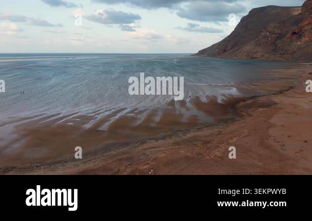 Wide coastal landscape with calm blue sea, wet sandy shore and rugged ...