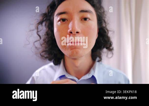 Smiling young man looks into camera while adjusting shirt collar with ...
