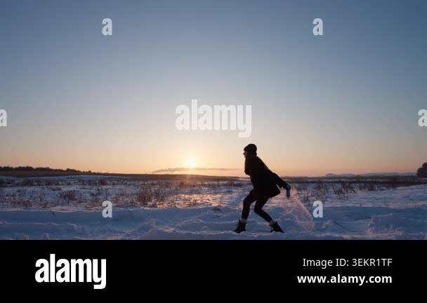 Silhouette of a woman in a snowy field at sunset in the winter ...