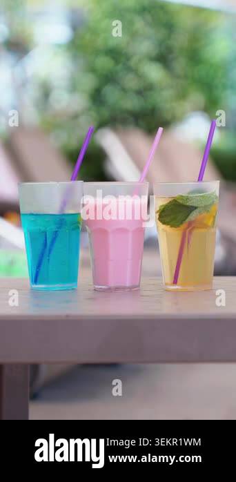 Side view of three colorful cold drinks with straws on poolside table ...