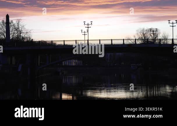 People and cars commuting on an arched bridge structure over quiet ...